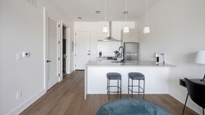Uma cozinha moderna com uma ilha central, dois bancos altos, iluminação pendente e vista para a área de jantar adjacente.