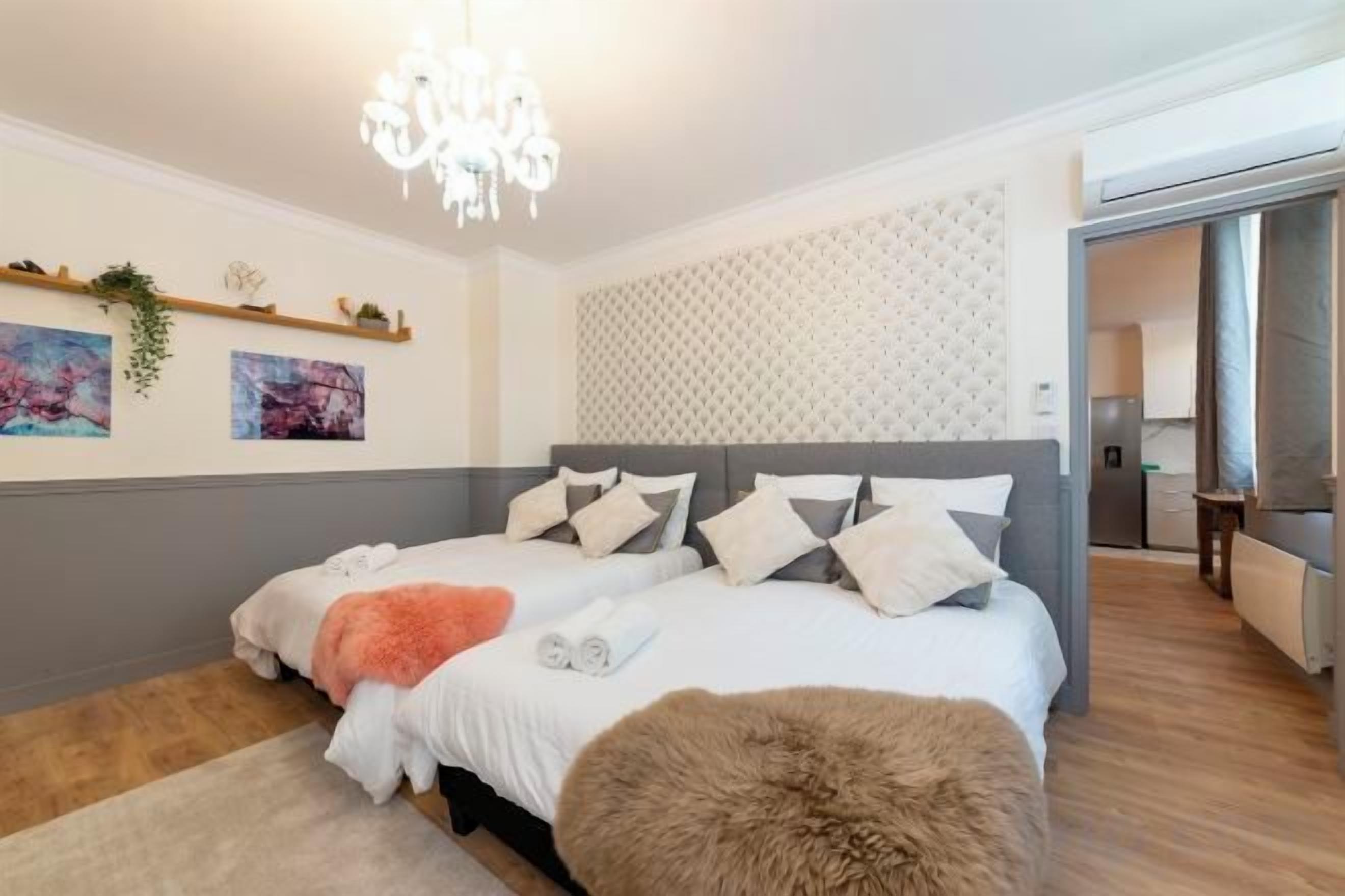 Quarto com cama de casal, lustre, tapete pequeno e um otomano macio.