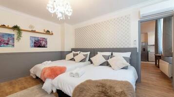 Quarto com cama de casal, lustre, tapete pequeno e um otomano macio.