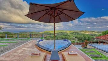 Área de hidromassagem com um guarda-sol grande, cadeiras de descanso e vista para a paisagem.