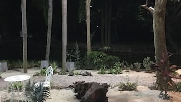 Área externa com mesa e cadeiras, cercada por árvores e plantas.