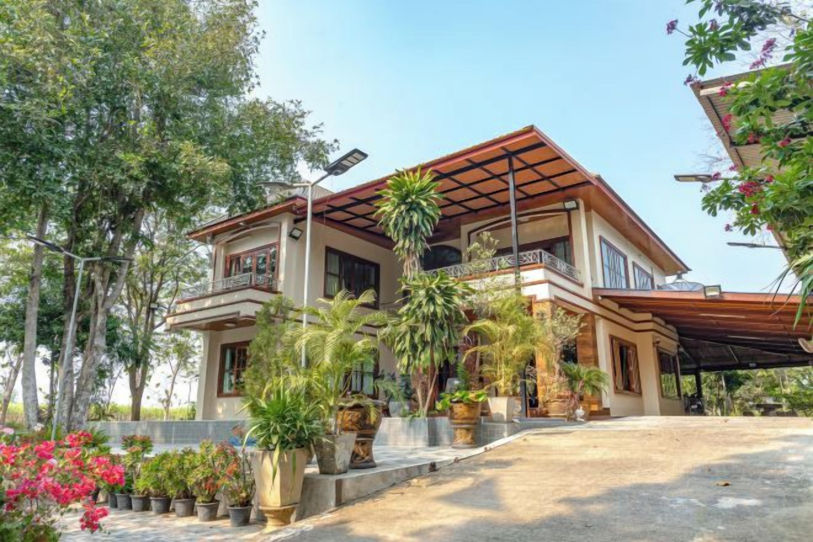 Uma casa de dois andares com varanda coberta, várias sacadas e um jardim com vasos de plantas.