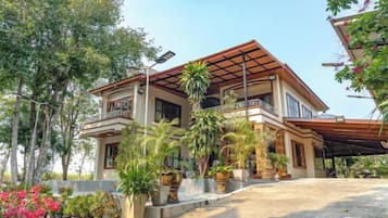 Uma casa de dois andares com varanda coberta, várias sacadas e um jardim com vasos de plantas.