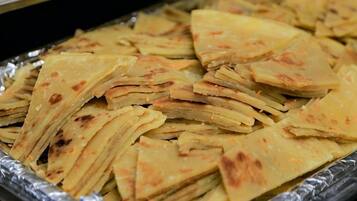 Uma bandeja com porções triangulares de comida, possivelmente um tipo de pão achatado, dispostas sobre uma superfície forrada com papel alumínio.
