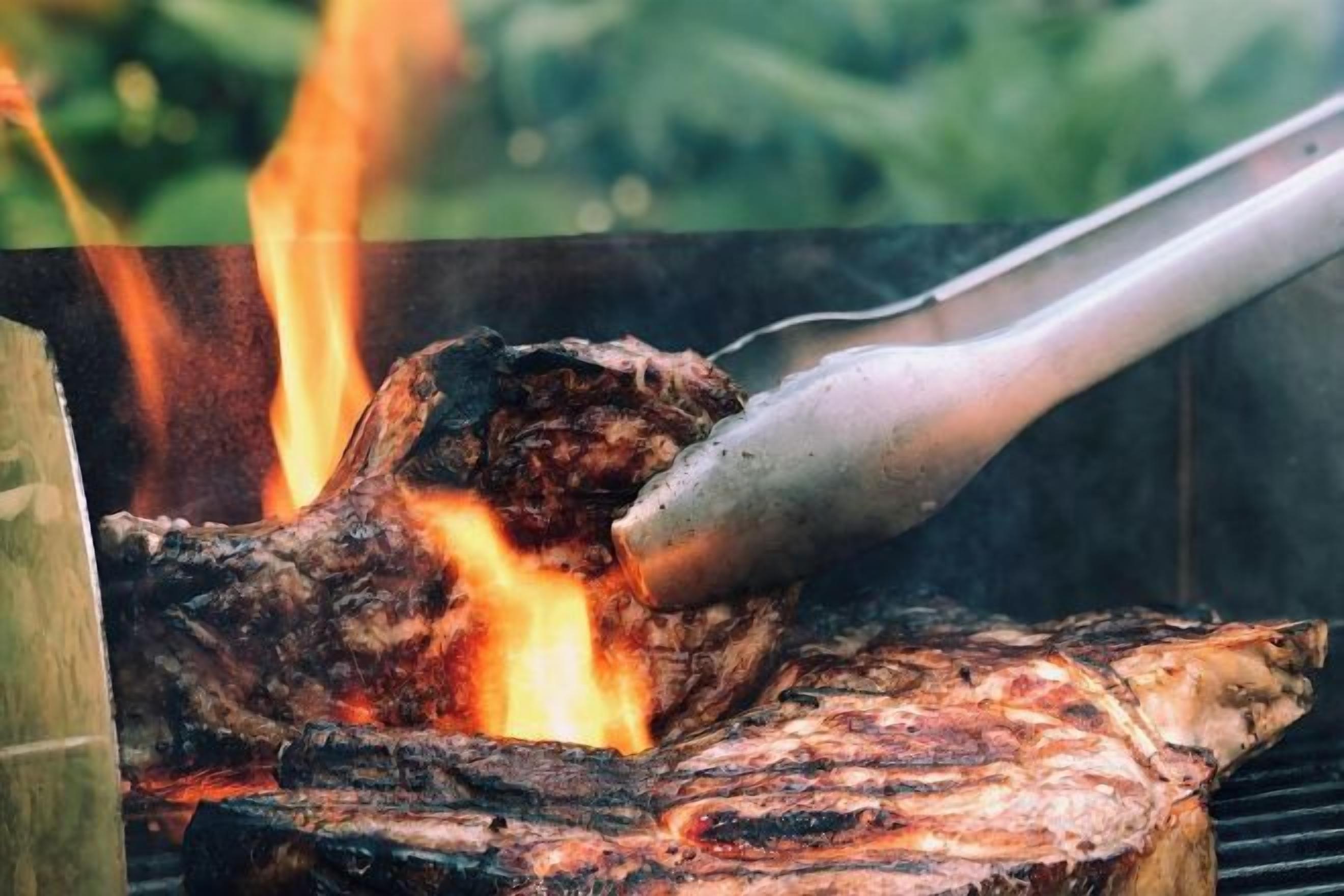 Uma churrasqueira com um bife sendo assado em chamas abertas.