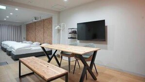 Quarto de hotel moderno com cama, mesa de madeira, um banco, televisão e guarda-roupa.
