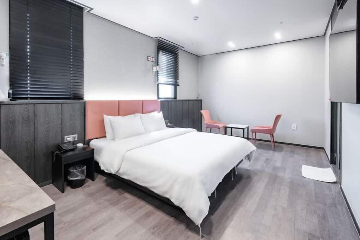 Quarto de hotel moderno com uma cama grande, uma mesa pequena, uma cadeira e uma escrivaninha.
