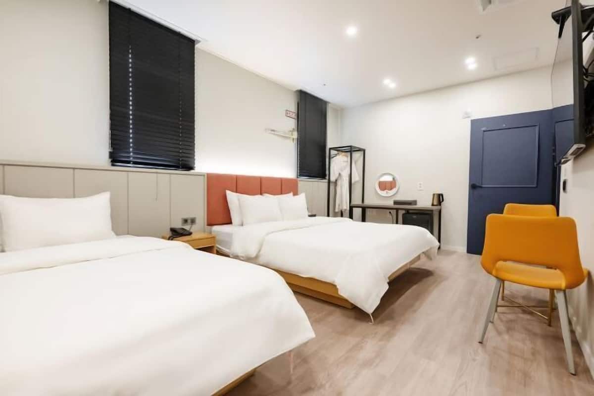 Quarto de hotel com duas camas, uma escrivaninha, uma cadeira e um guarda-roupa.