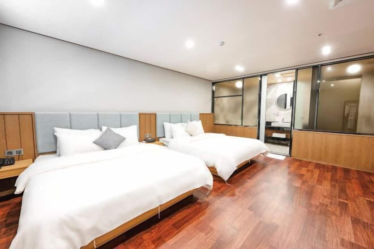 Quarto de hotel moderno com duas camas, piso de madeira e uma grande janela com vista.
