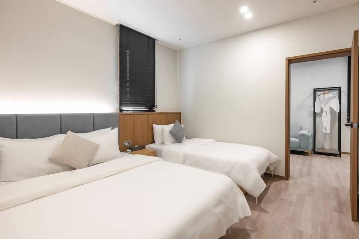 Quarto de hotel com duas camas, cabeceira de madeira, mesa de cabeceira pequena e porta para um banheiro.