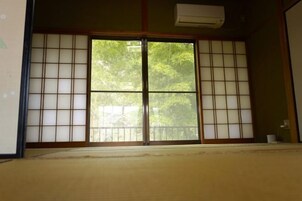 Um quarto japonês tradicional com tatames, portas deslizantes com biombos de papel e vista para o verde lá fora.