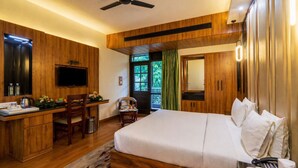 Quarto de hotel com cama, escrivaninha, cadeiras e televisão.