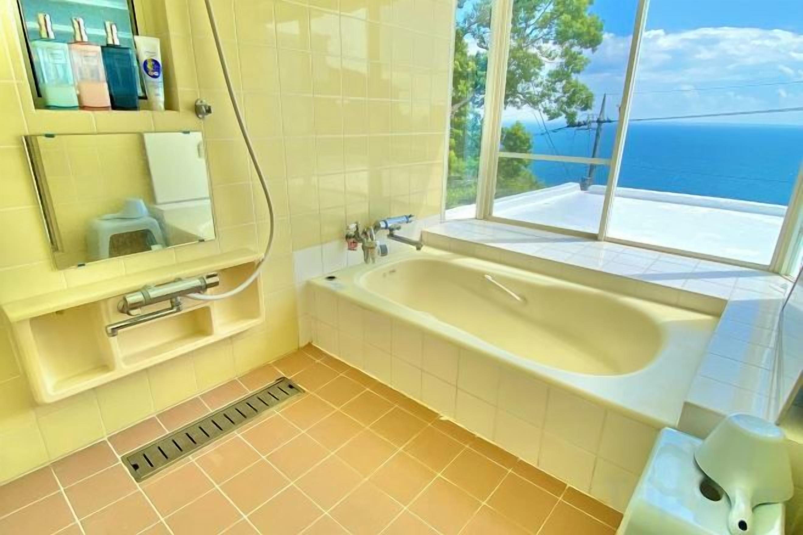 Casa de banho com banheira, janela com vista para o mar e prateleira com artigos de higiene pessoal.