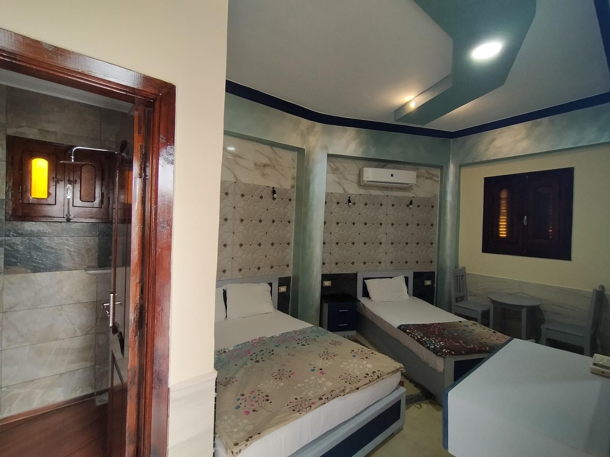 Quarto de hotel com duas camas, chuveiro, uma pequena mesa e ar condicionado fixado na parede.