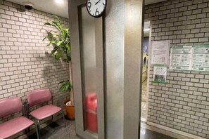 Uma sala de espera com relógio, cadeiras e cartazes informativos nas paredes.