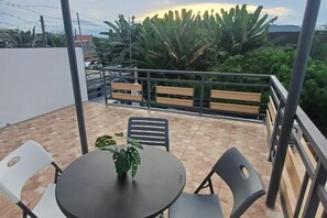 Uma varanda com mesa redonda e cadeiras, um vaso de planta e um banco de madeira.