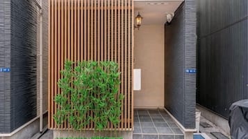 Uma entrada estreita com parede de ripas de madeira vertical, um pequeno vaso com plantas verdes e chão de azulejos.