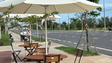 Mobiliário de exterior com guarda-sóis, um passeio pavimentado e uma estrada ao fundo.