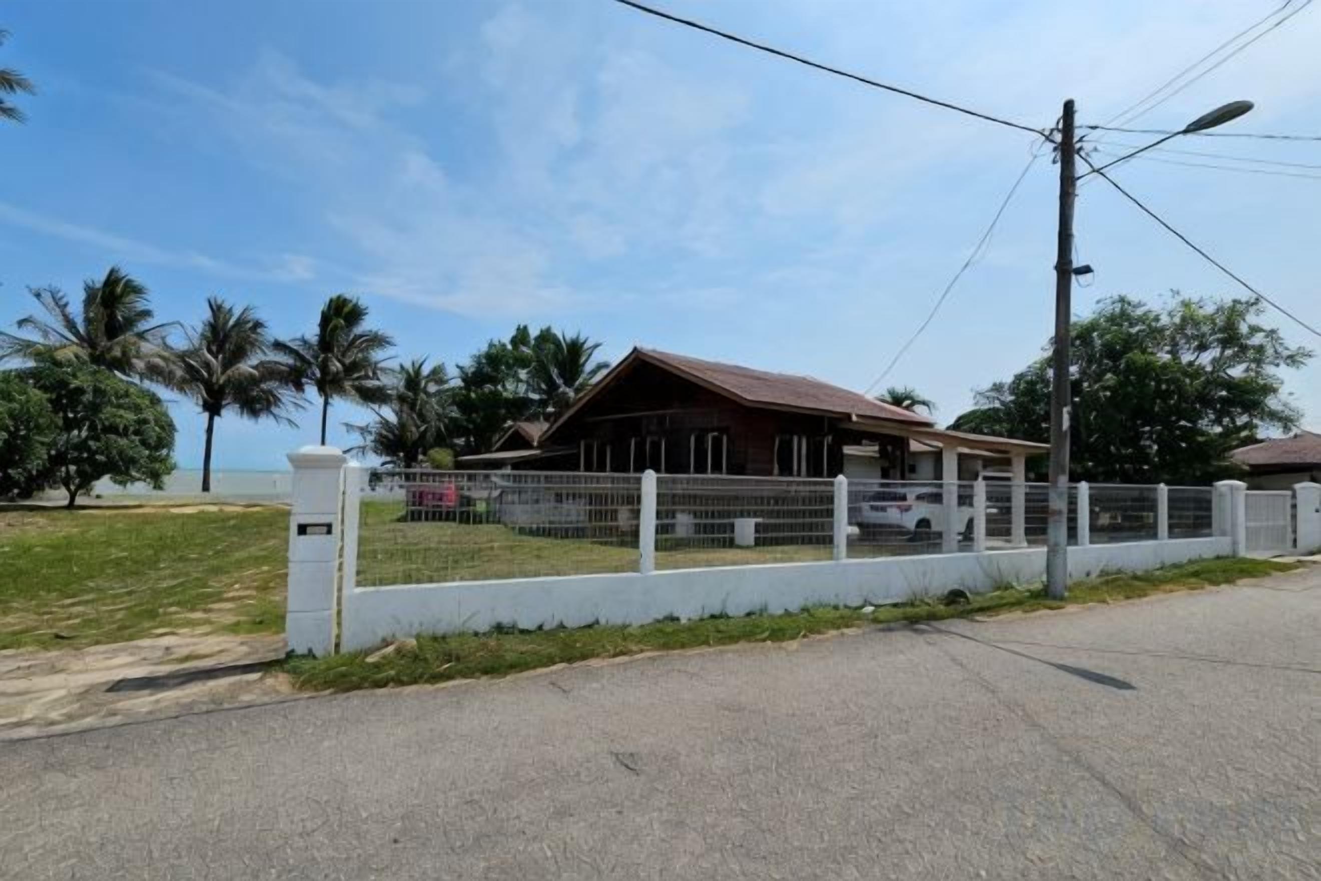 Uma casa com um quintal cercado, uma rua pavimentada na frente e um céu limpo.