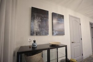 Um corredor com um console preto, uma tigela e duas pinturas abstratas na parede.