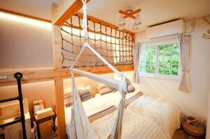 Quarto com cama rede, escada de madeira, janela com cortinas e ventilador de teto.