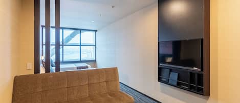 Quarto de hotel moderno com sofá, mesa pequena, TV na parede e janela com vista para a cidade.