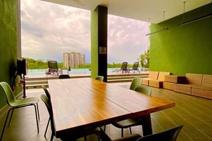 Quarto com mesa e cadeiras de madeira, um sofá e vista para uma piscina e edifícios.