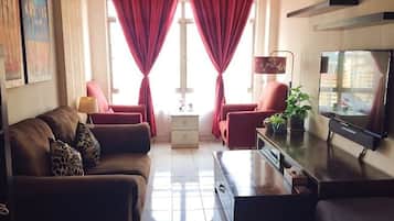 Uma sala de estar com sofá, cadeiras, televisão e uma pequena mesa.
