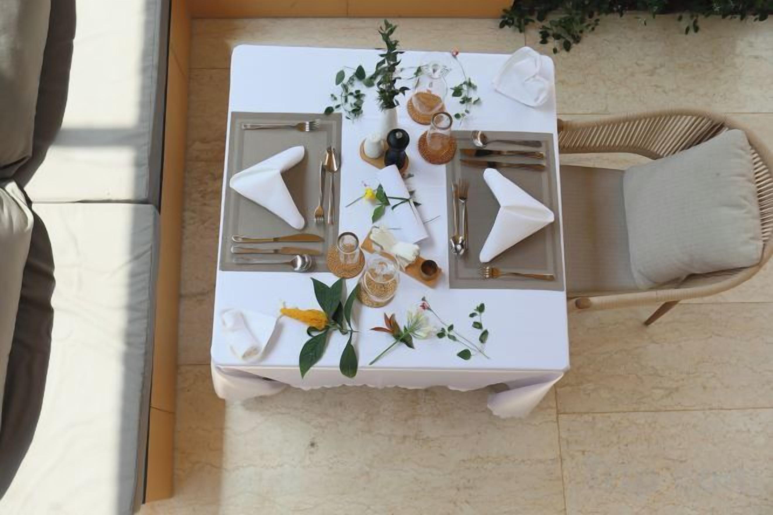 Mesa de jantar posta com louça branca, um vaso com flores e uma garrafa de vinho.