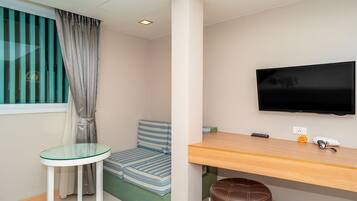 Quarto com cama, televisão, mesa pequena, cadeira e janela com cortinas.