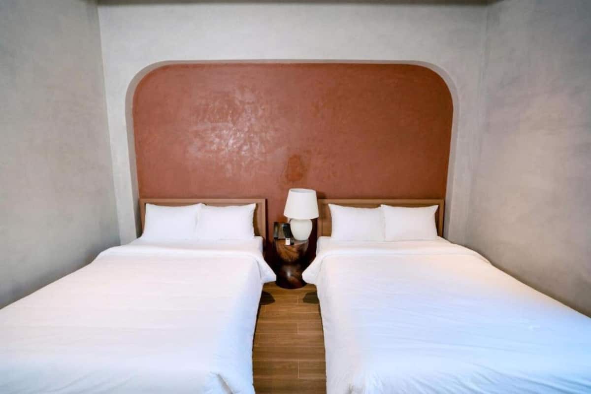 Quarto duplo com duas camas, uma cabeceira de madeira e uma mesa de cabeceira com abajur.