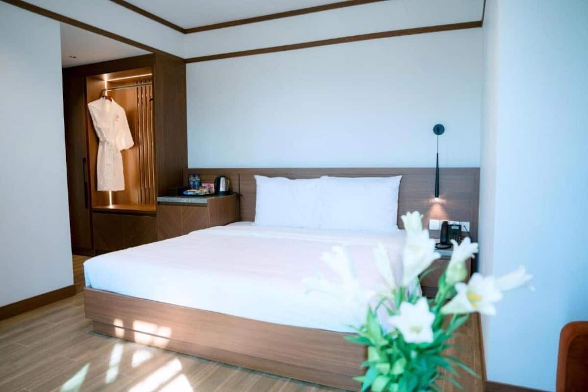 Quarto de hotel com uma cama grande, uma mesinha de cabeceira com abajur, e um roupão pendurado na porta.
