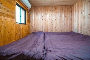 Quarto com paredes de madeira, uma cama com colcha roxa e uma janela com vista.