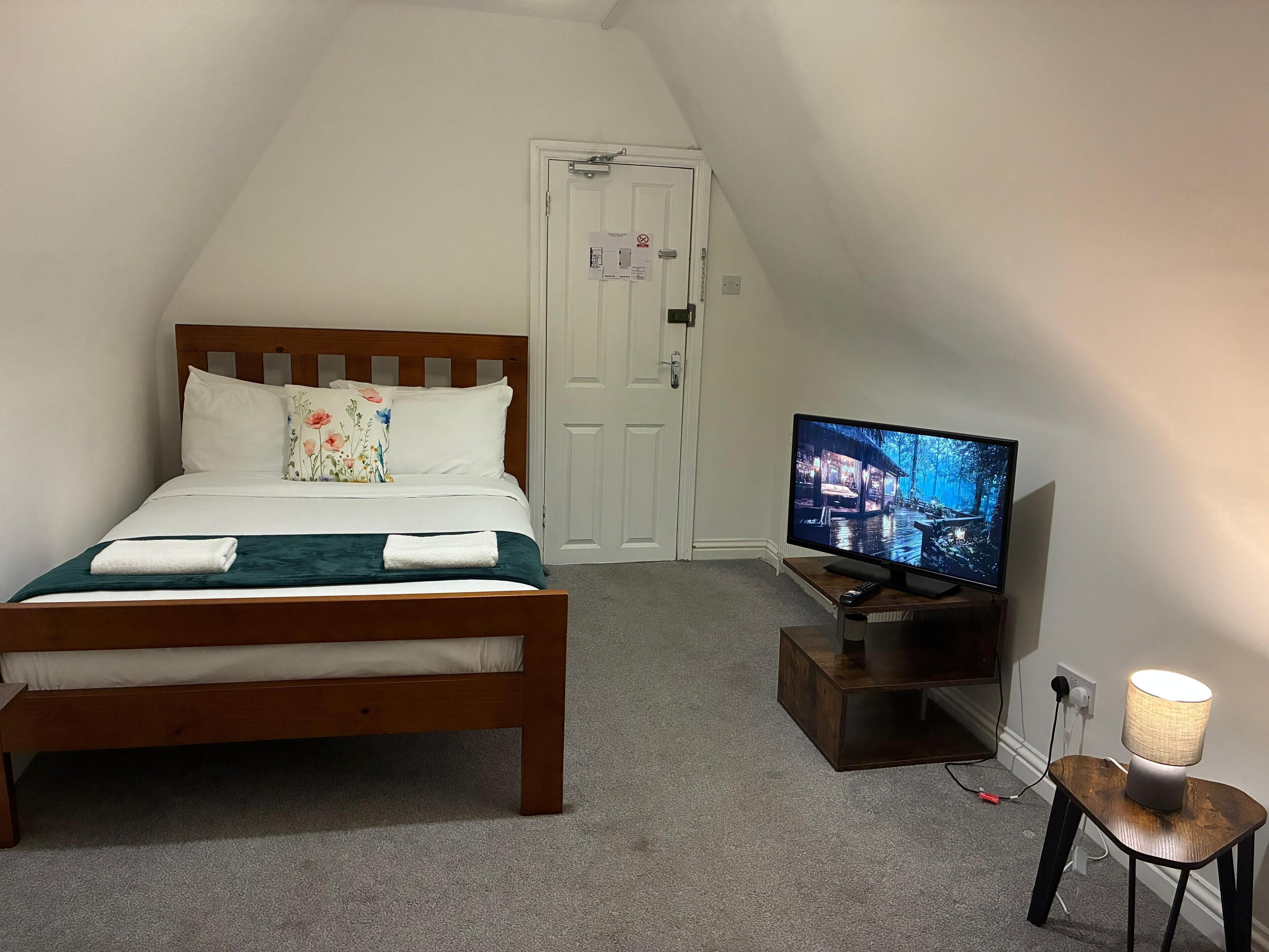Quarto com cama de madeira, televisão em um móvel e abajur sobre uma mesinha.