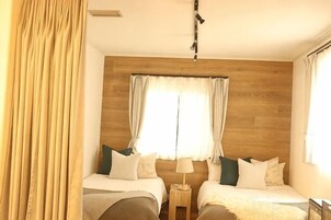 Quarto de hotel com duas camas, cabeceira de madeira, cortinas, mesa de cabeceira e abajur.