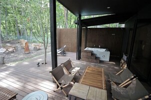Um deck externo com móveis de madeira, uma banheira de hidromassagem e vista para as árvores ao redor.