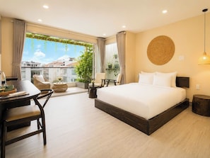 Quarto de hotel com uma cama grande, uma escrivaninha, uma cadeira, um adorno circular de fibras na parede e vista para edifícios pela janela.