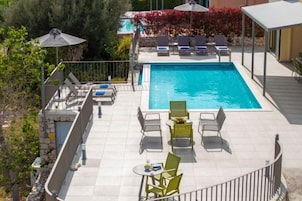 Piscina cercada por espreguiçadeiras e mesas, com um pátio revestido de azulejos.