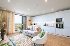 Sala de estar moderna com sofá, poltrona e vista da cidade através de amplas janelas.