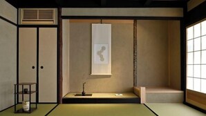 Um quarto japonês tradicional com tatames, um painel shoji, uma mesa baixa com um vaso e uma obra de arte pendurada.