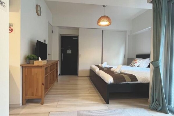 Quarto com cama, cómoda de madeira, televisão e luminária pendente.