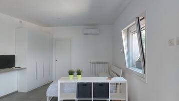 Quarto com parede branca, janela, radiador, armário branco e televisão.