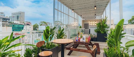 Terraço no telhado com área de estar coberta, plantas em vasos e vista para a paisagem urbana.