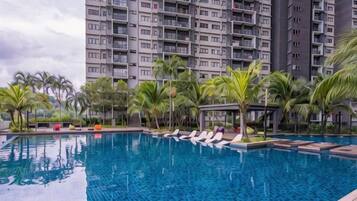Piscina com espreguiçadeiras, palmeiras e um edifício alto ao fundo.
