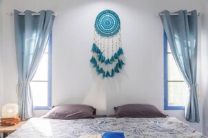 Quarto com cama, duas almofadas, mesa de cabeceira, abajur e um objeto decorativo na parede.