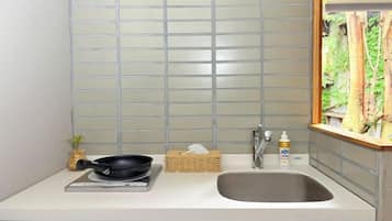Cozinha com pia, janela com vista para árvores e uma pequena planta no balcão.