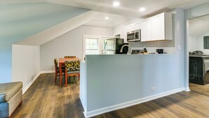 Uma cozinha moderna com armários brancos, micro-ondas embutido e um espaço de jantar com mesa e cadeiras de madeira.
