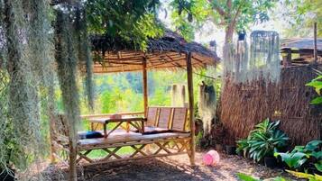 Um gazebo de madeira com telhado de palha, rodeado por vegetação exuberante e plantas.