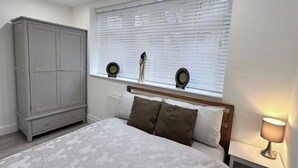 Quarto com cama, mesa de cabeceira com abajur, guarda-roupa e janela com persianas.