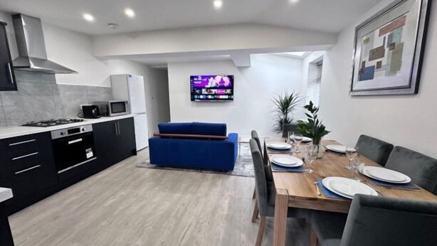 Uma cozinha moderna com área de refeições, uma televisão de tela plana na parede e um sofá azul.
